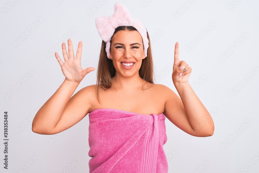 Beautiful young woman wearing pink shower towel and beauty headband over white background ...