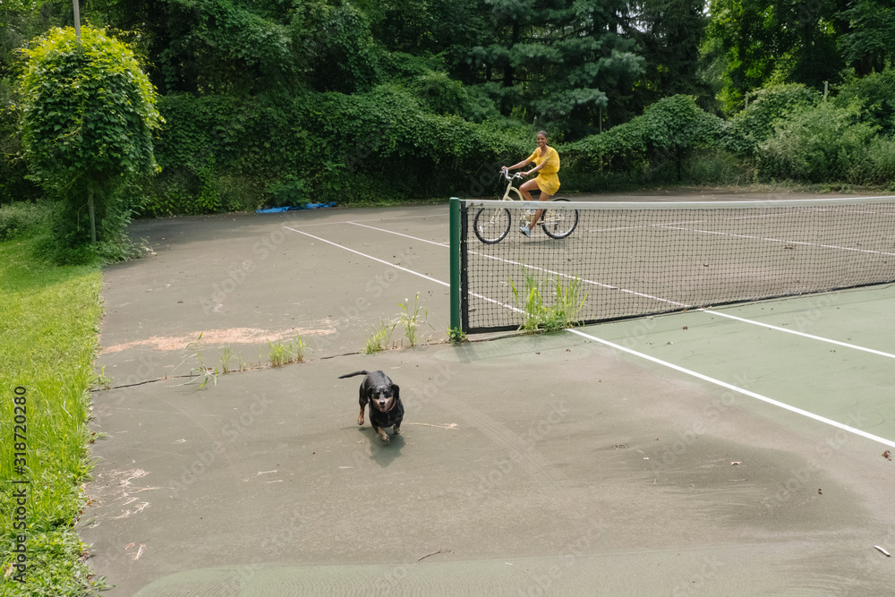 African American woman riding bike with dog on tennis court during ...