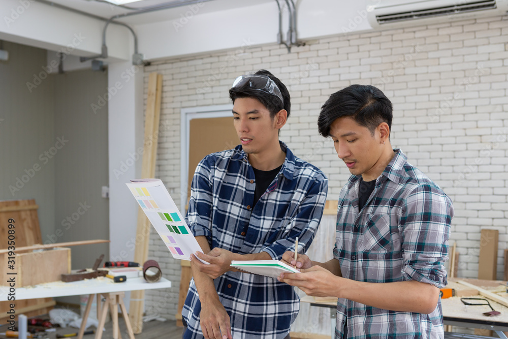 Two young asian carpenters holding paint color sample chart and ...