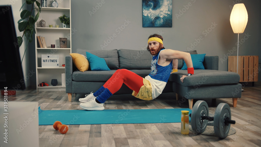 Handsome silly sportsman doing exercise leaning on a sofa watching ...