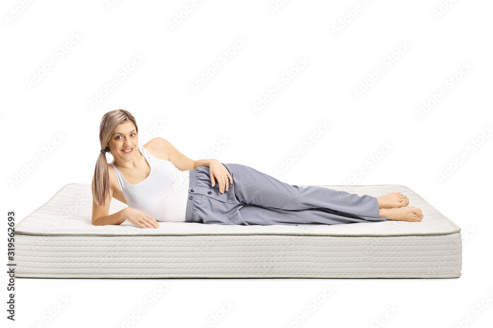 Young woman lying on a bed mattress in pajamas and smiling at the ...