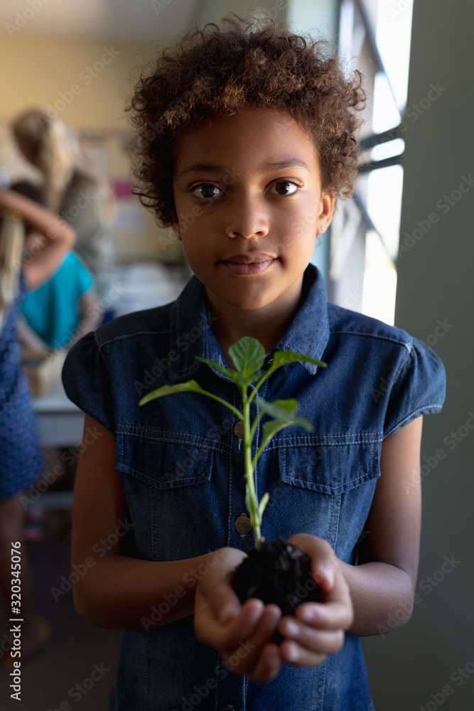 Schoolgirl standing holding a seedling plant in a jar of earth in an ...