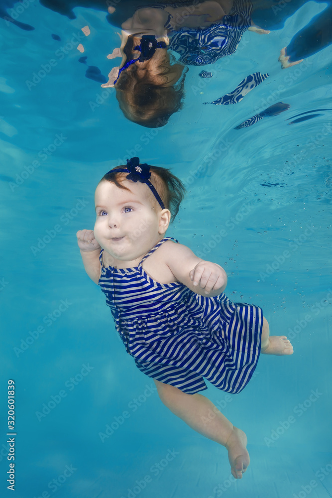 Cute chubby little girl in a sundress dives underwater in a swimming ...