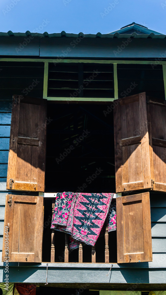 Batik fabric hanging on the window of Rumah Kampung under the bright ...