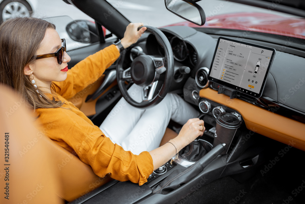 Young and cheerful woman driving sports car with a digital touchscreen ...