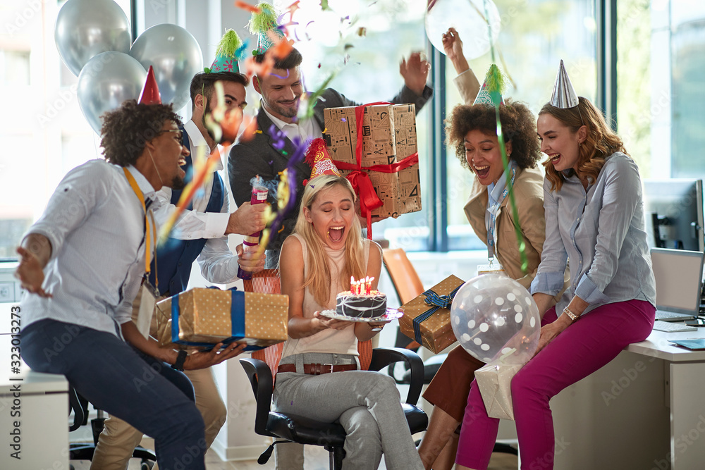 group of colleagues surprising female colleagues with birthday cake and ...
