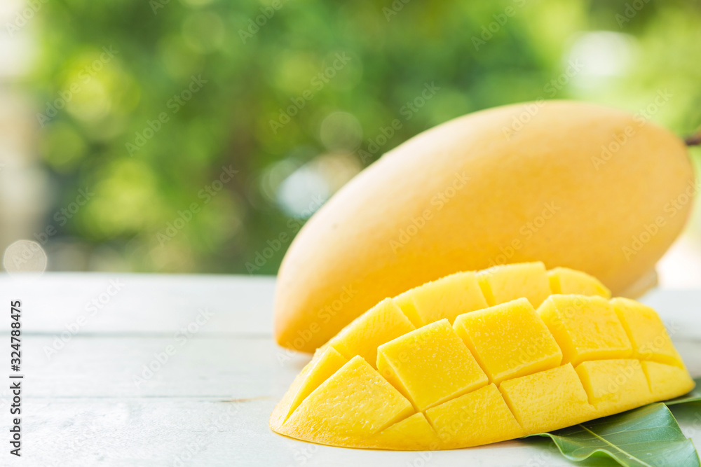 Sweet yellow mangos and slided on white wooden table with green nature ...