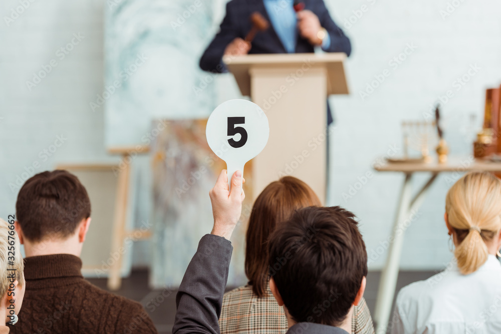 back view of buyer showing auction paddle with number five during ...