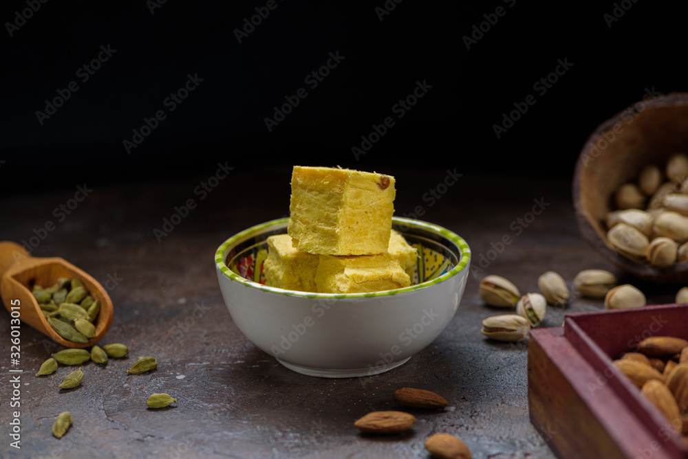Soan papdi dessert cubes in bowl, cardamom grains in wooden scoop ...