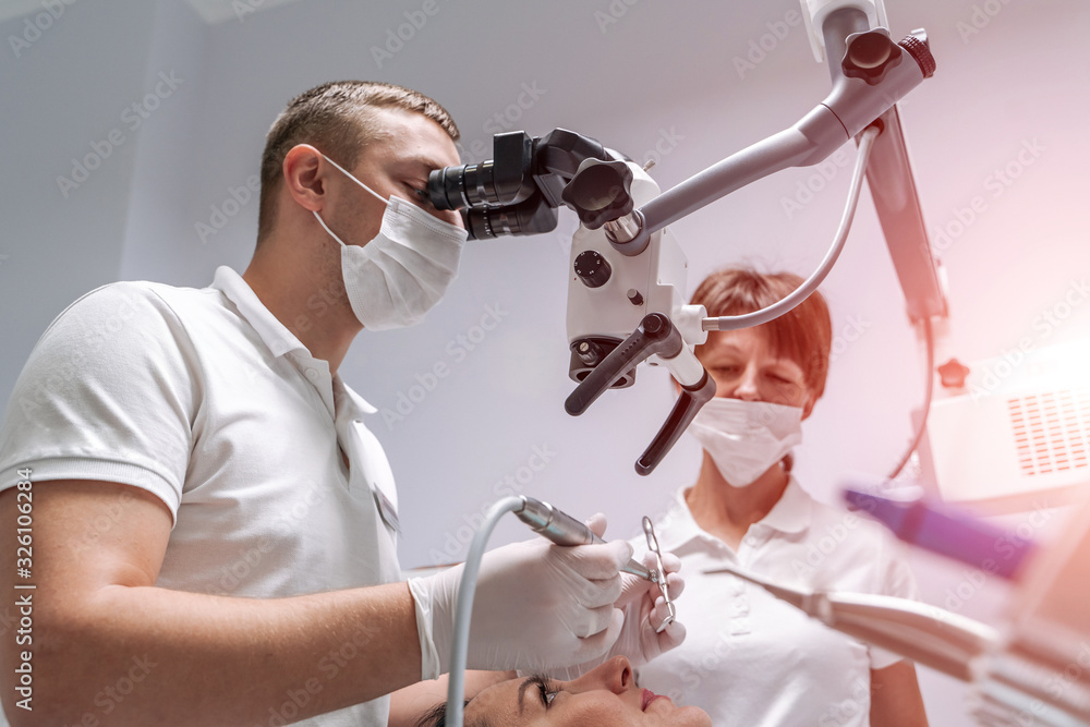 Dentist curing a female patient's teeth with a microscope in the ...