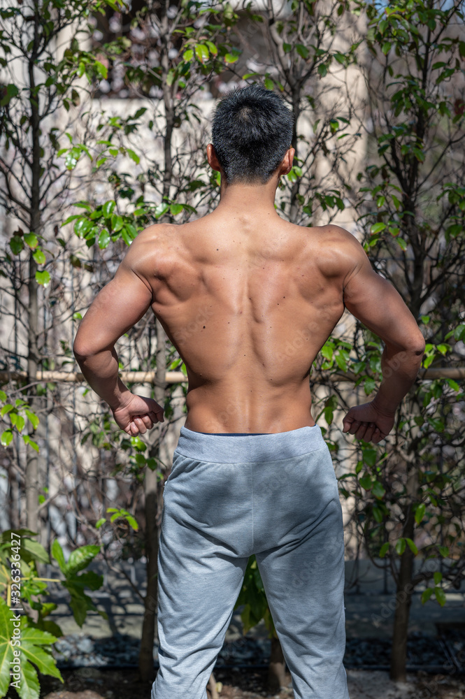 A young Asian amateur bodybuilder poses shirtless outdoors showing off ...