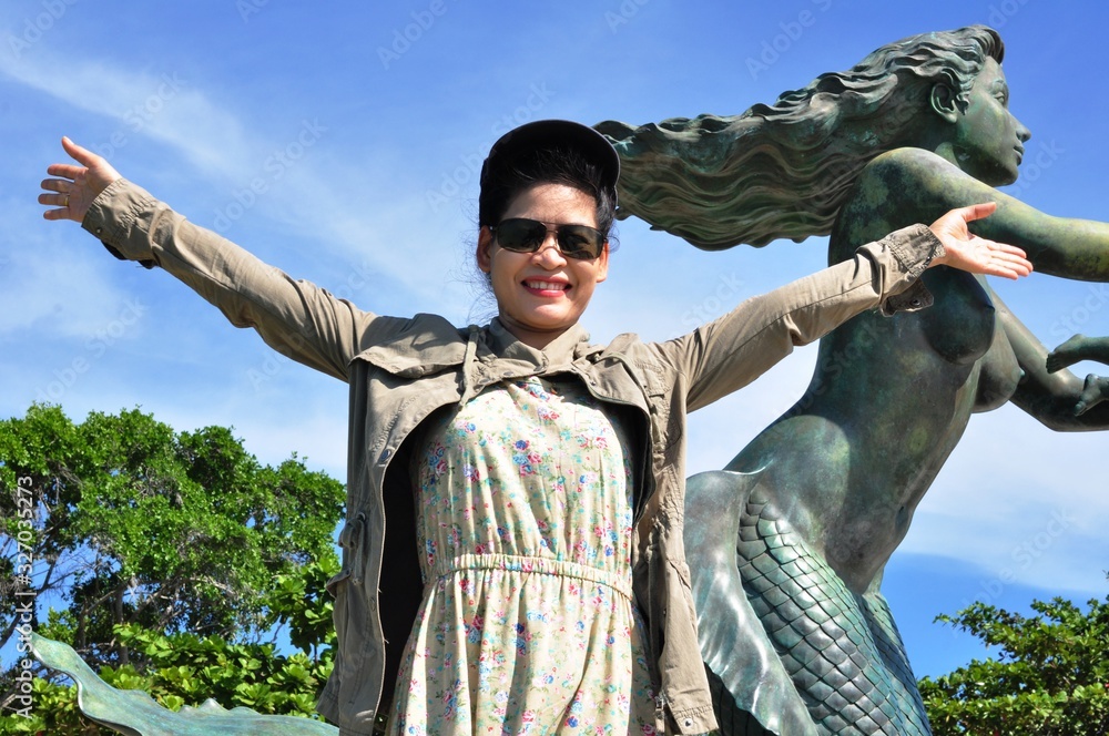 Beautiful girl with a statue of a mermaid and a son That overlooks the ...