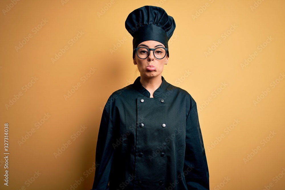 Young beautiful brunette chef woman wearing cooker uniform and hat over ...