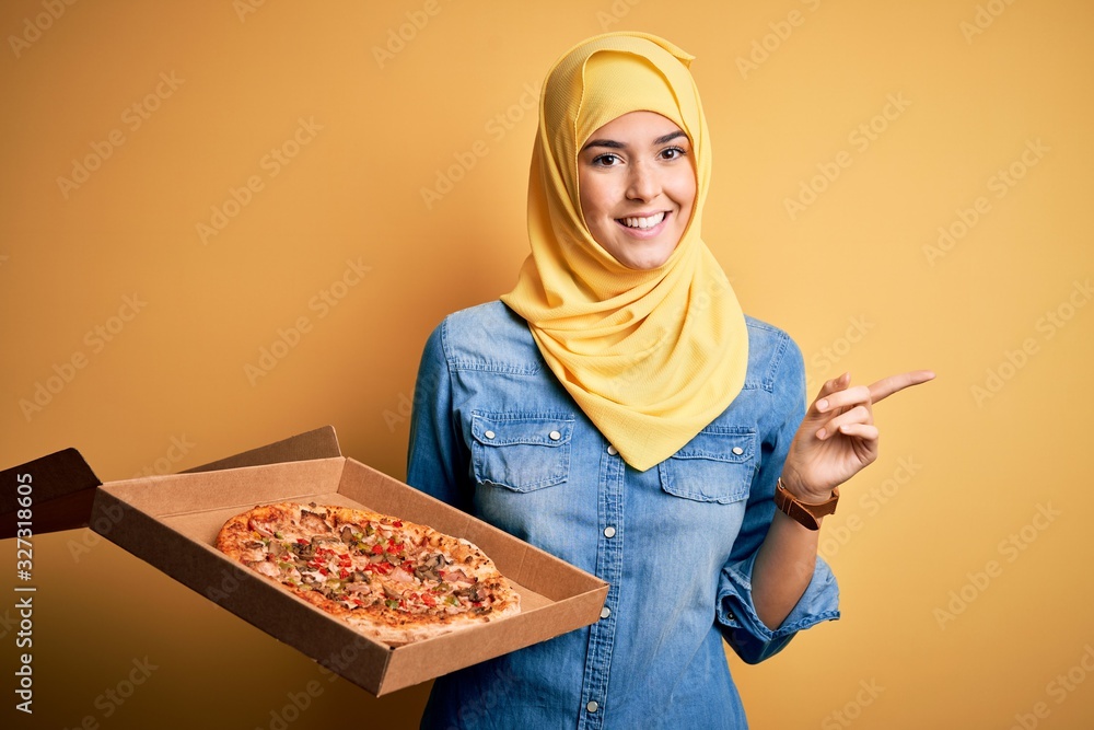 Young girl wearing muslim hijab holding box with Italian pizza over ...