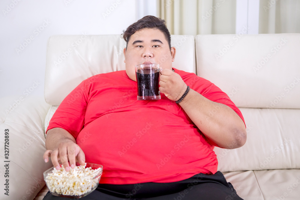 Fat man sipping a cola while grabbing popcorns Stock Photo | Adobe Stock