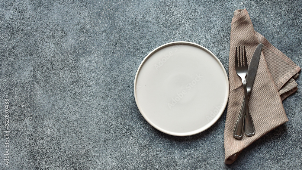 White craft plate, cutlery and napkin on dark stone table. Top view ...