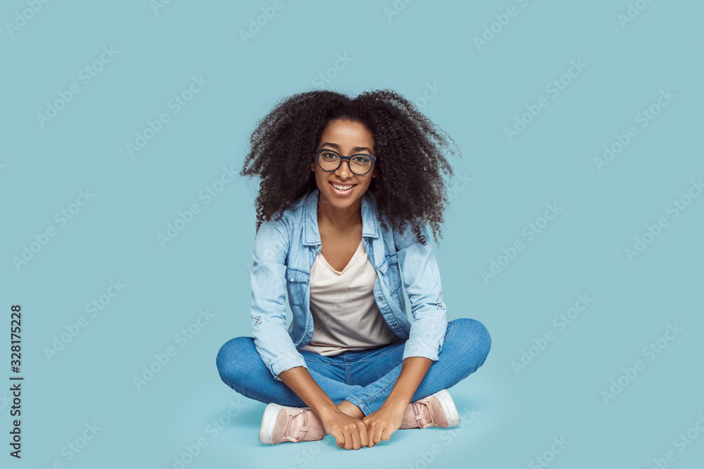Freestyle. African girl in glasses sitting isolated on gray leaning ...