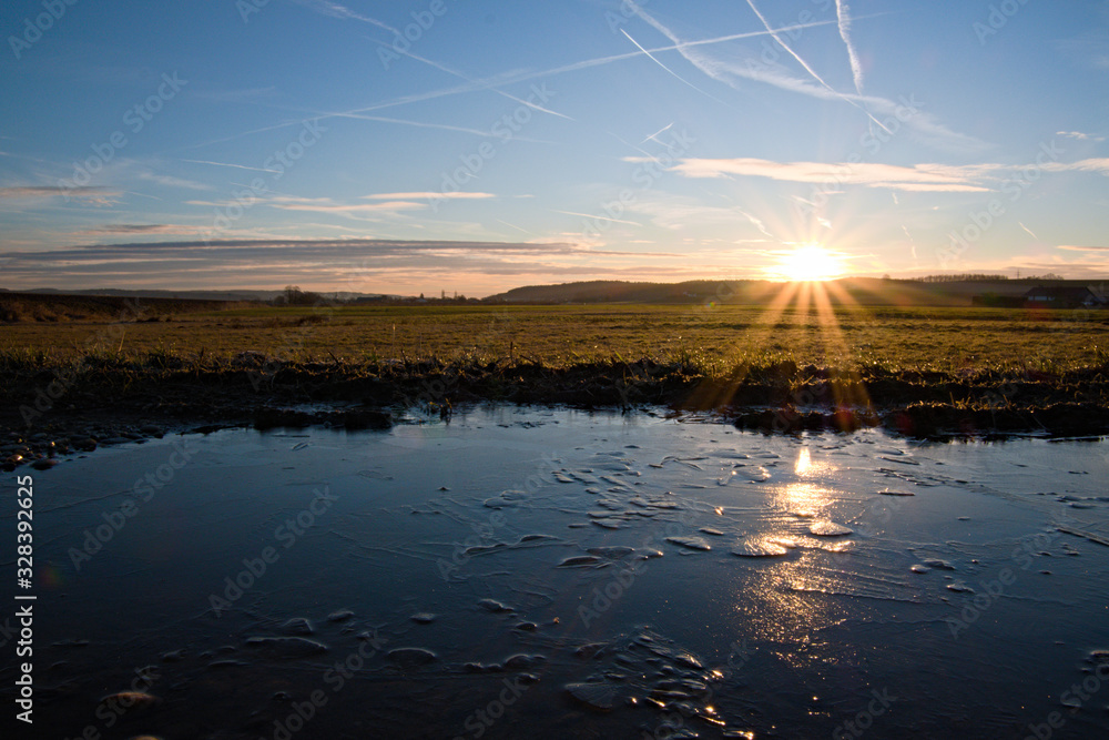 Sunrise reflected on a frozen puddle with beautiful blue and pink ...