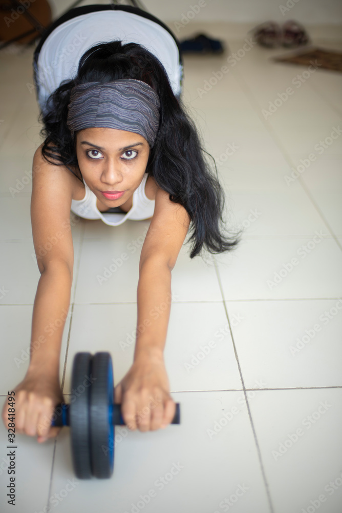 Indian brunette girl in sportswear performing exercise with ab roller ...