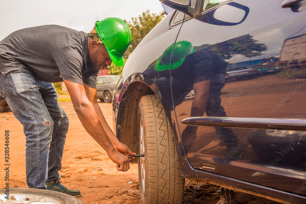 young african man, a professional mechanic, trying to change a car tyre ...
