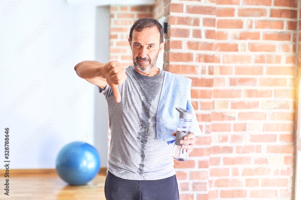 Middle age handsome sportman sweaty holding bottle of water and towel ...