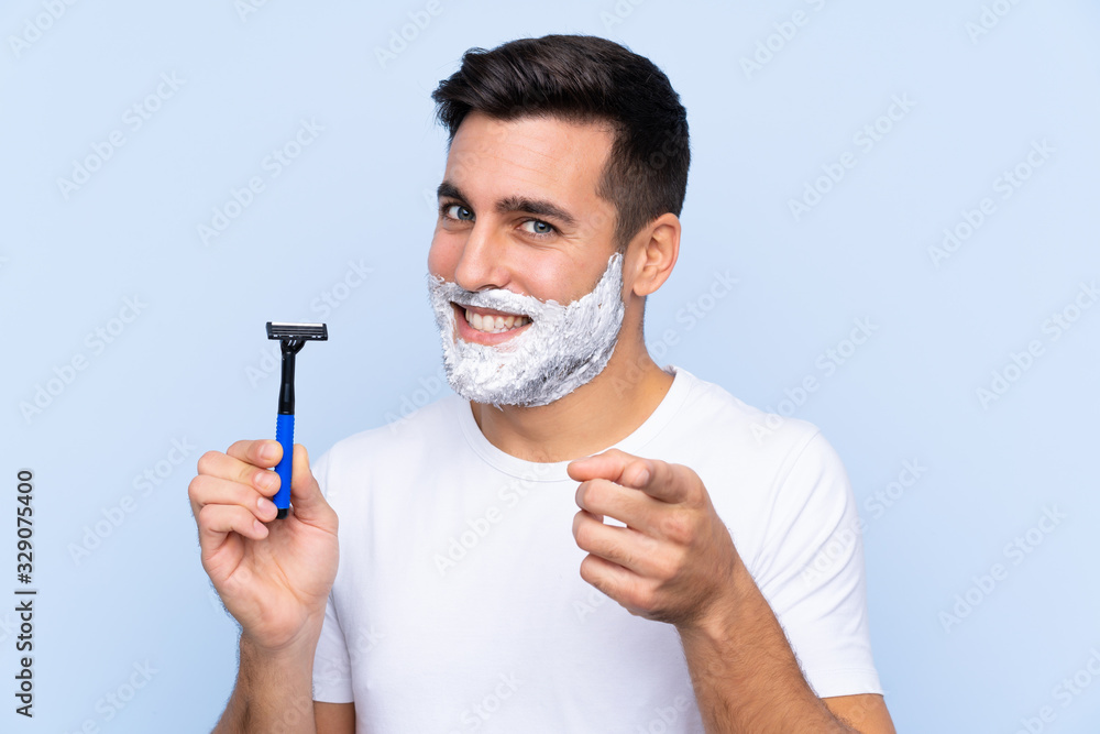 Young handsome man shaving his beard over isolated background points ...
