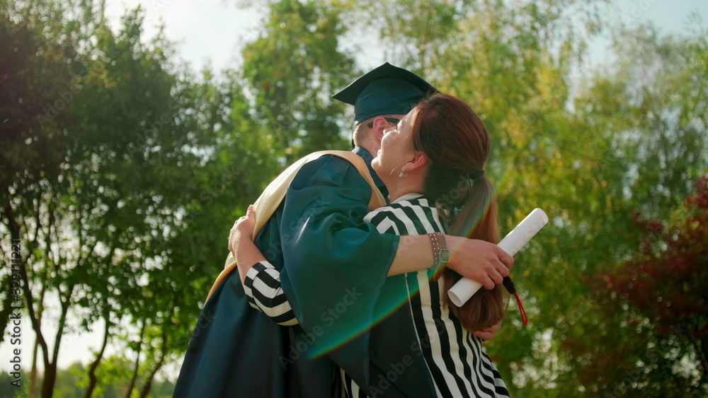 Excited Graduate Student in Gown and Cap with Diploma Hugs his Friend ...