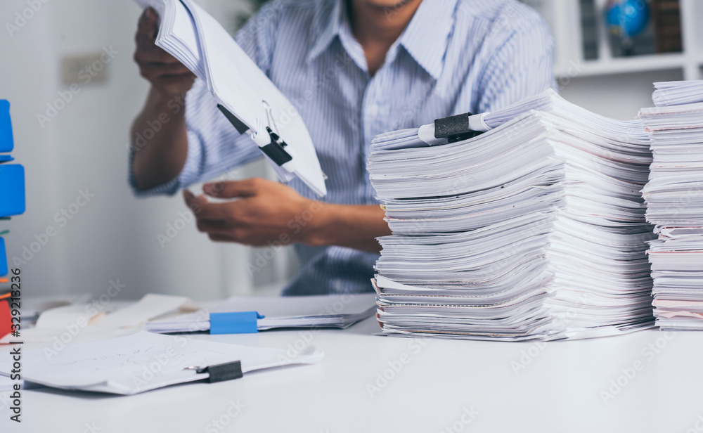 Young asian exhausted businesssman with messy desk and stack of papers ...