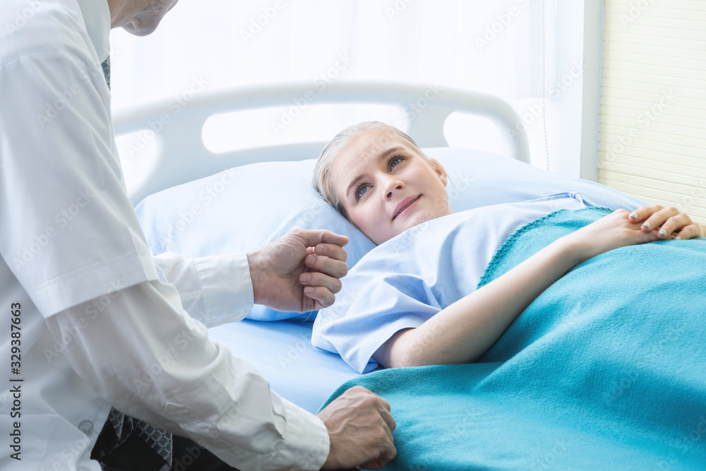 Young woman patient lying in bed while doctor visit and talking about ...