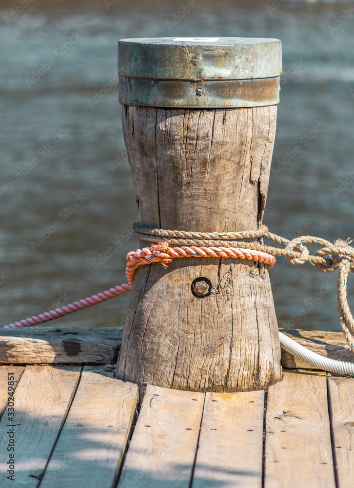 A rope is tied to a wooden mooring bollard with the Yarra River ...