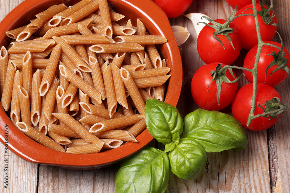 Primo piano di penne rigate integrali crude con pomodorini basilico e ...