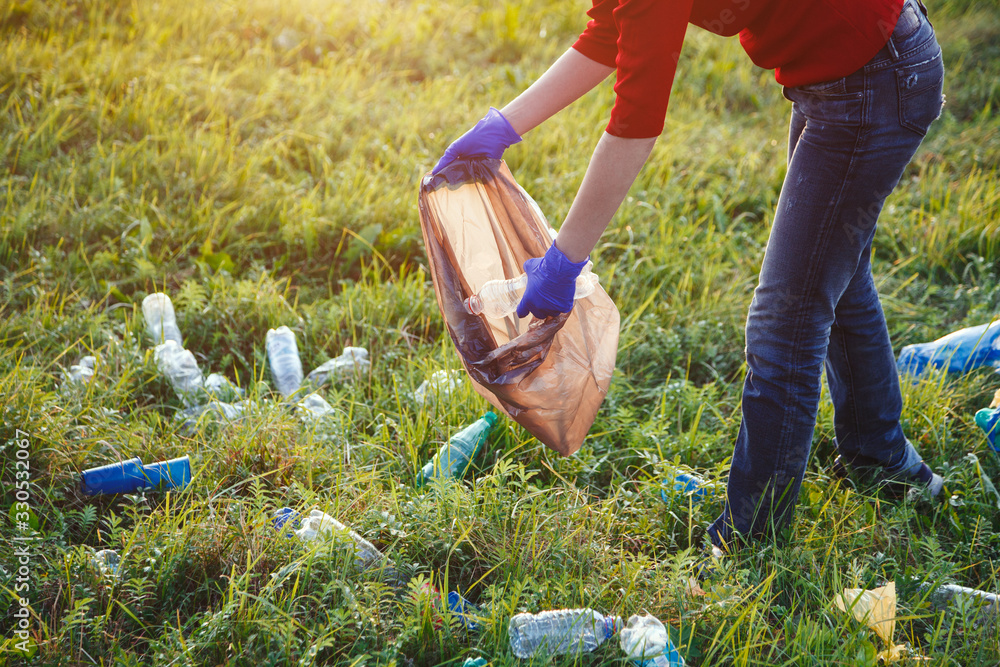 volunteer young woman collecting garbage, holding full bag of waste and ...