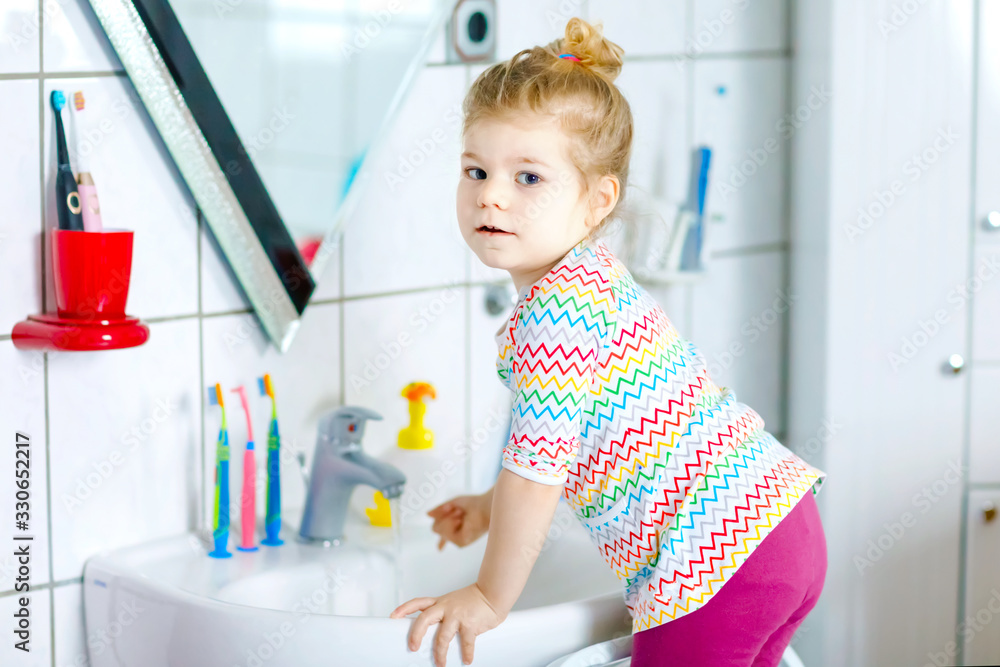 Cute little toddler girl washing hands with soap and water in bathroom ...