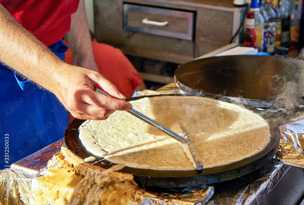 Making crepes pancakes at a market. A hand makes crepes on a metal ...