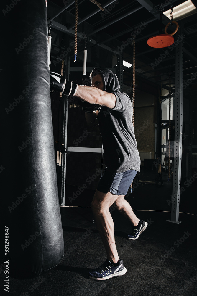 Professional boxer muscular man beats a punching bag in boxing gloves ...
