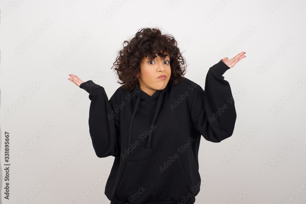 Puzzled and clueless young woman with arms out, shrugging her shoulders ...