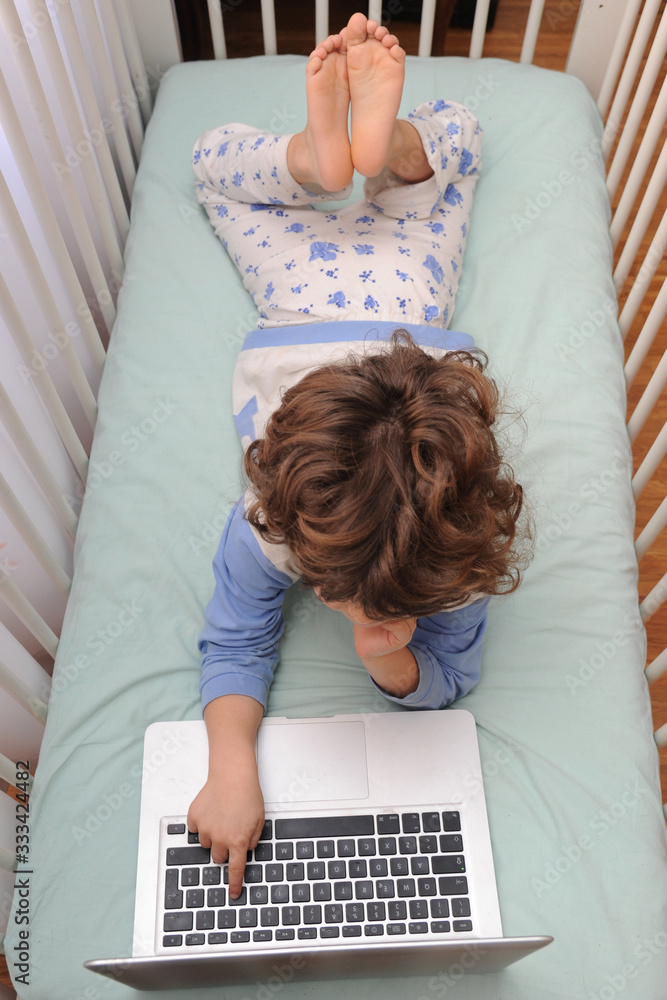 Young child 4 years old in the bed looks lap top computer during n ...