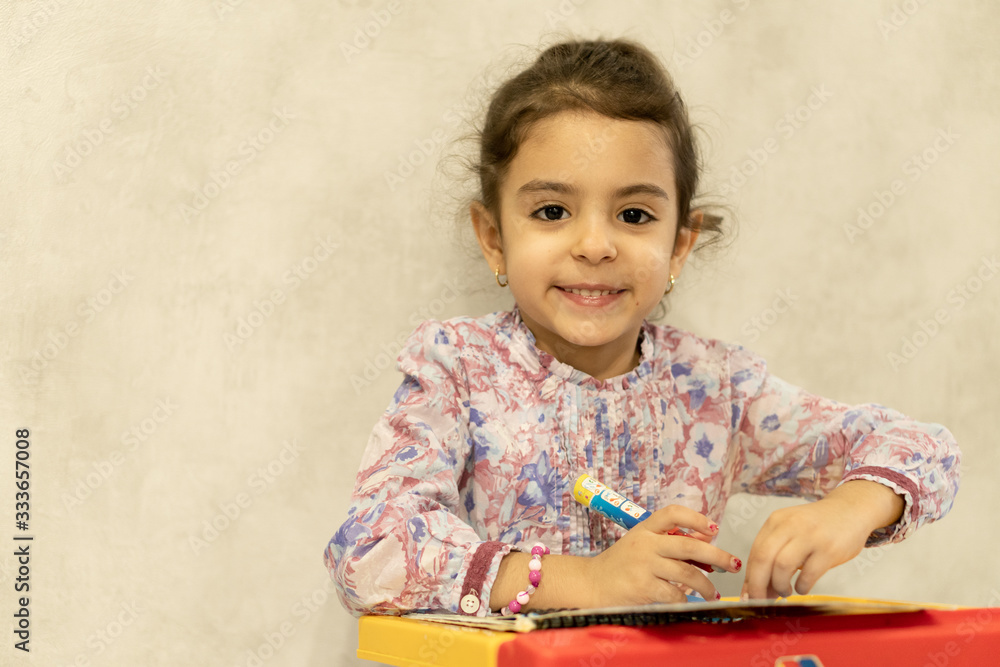 Little girl of Persian appearance draws sitting at desk. Beautiful girl ...