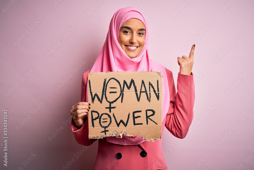 Young activist arab woman wearing pink muslim hijab holding banner with ...