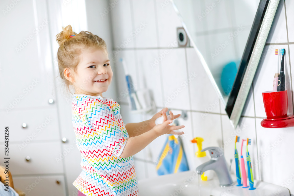 Cute little toddler girl washing hands with soap and water in bathroom ...