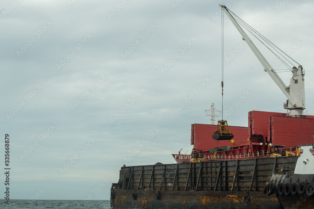 Loading coal from cargo barges onto a bulk vessel using ship cranes in ...