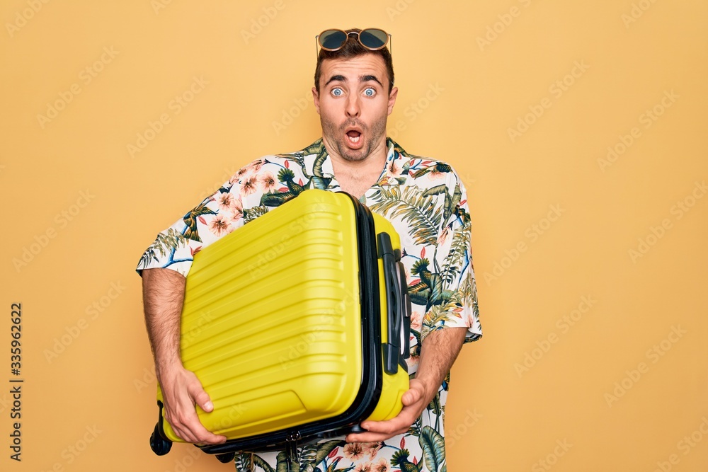 Handsome tourist man with blue eyes on vacation holding suitcase over ...