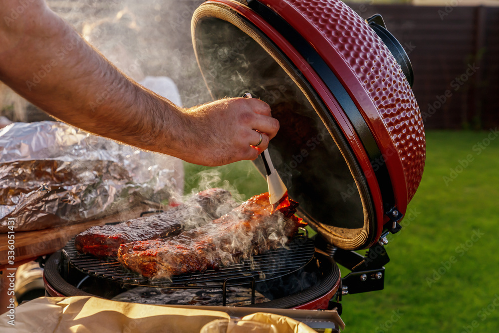 Red Ceramic Barbecue Grill. Smoke coming out of BBQ. The man coats ribs ...