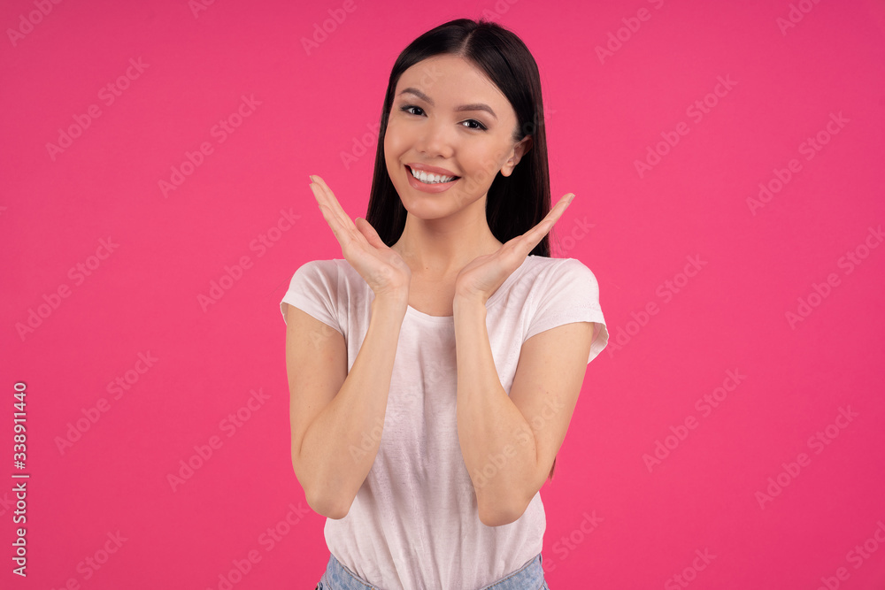 Pleasant looking Asian female model smiles gladfully, spreads palms ...