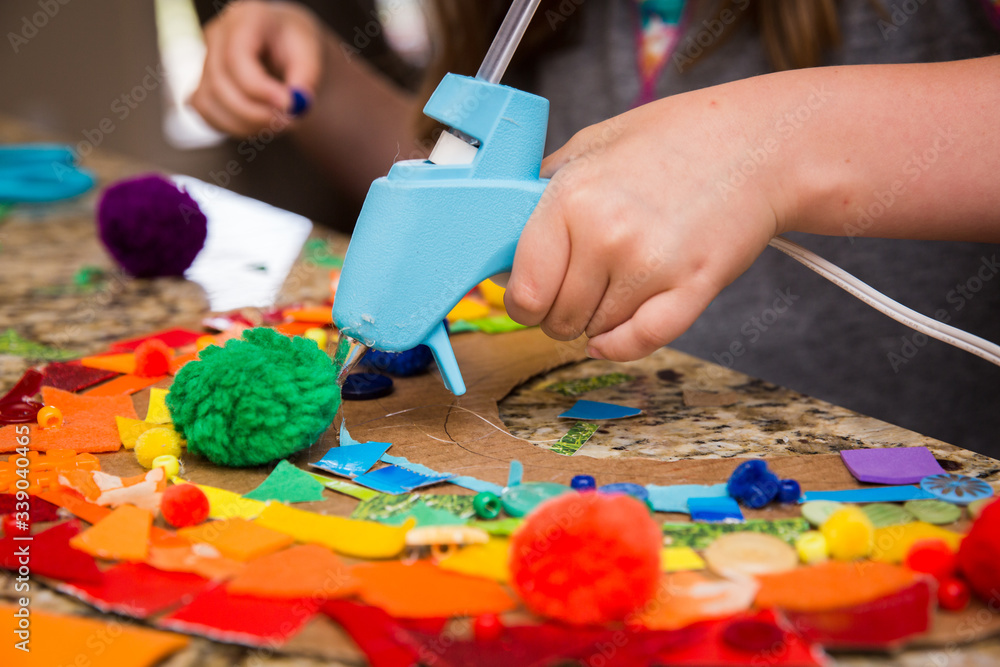 Child using hot glue gun to place object on a rainbow collage Stock ...