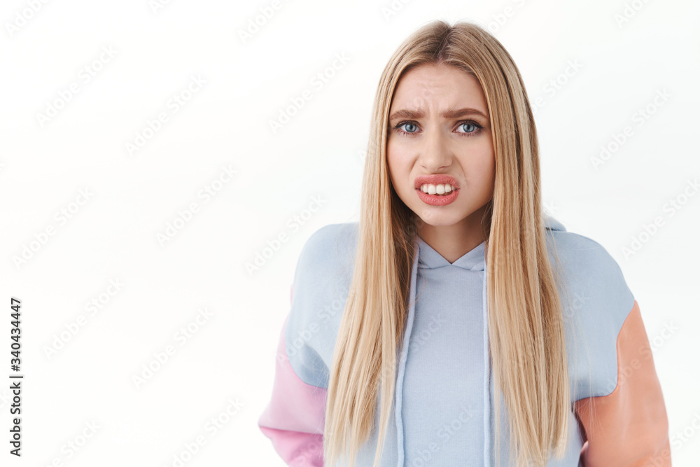 Close-up portrait of embarrassed blonde girl, stooping and clench fists ...