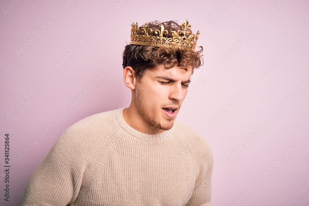 Young blond man with curly hair wearing golden crown of king over pink ...