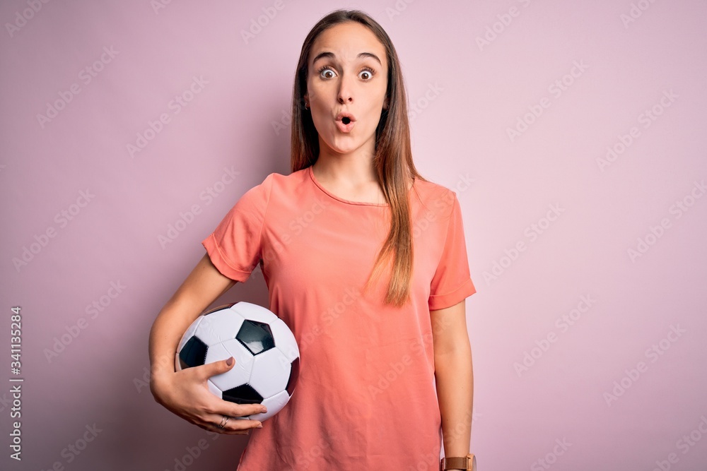 Young beautiful player woman playing soccer holding football ball over ...