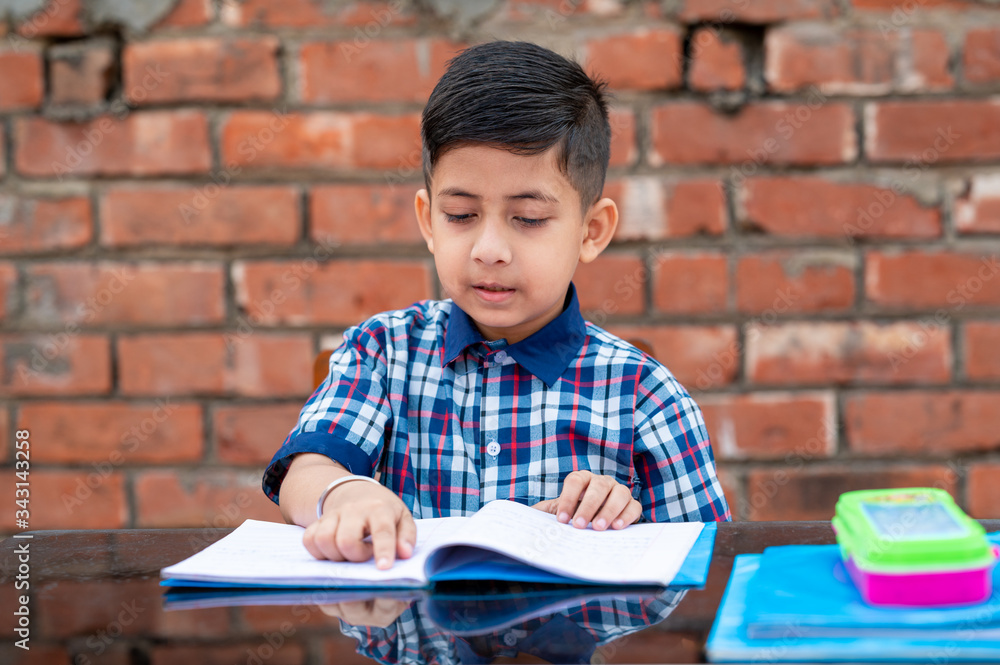 Primary school student in proper school uniform reading book on study ...