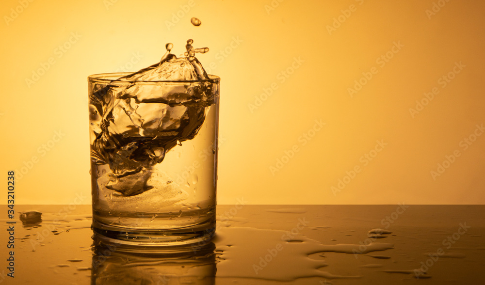 Splash of water in a glass with ice on a gold background. Female ...
